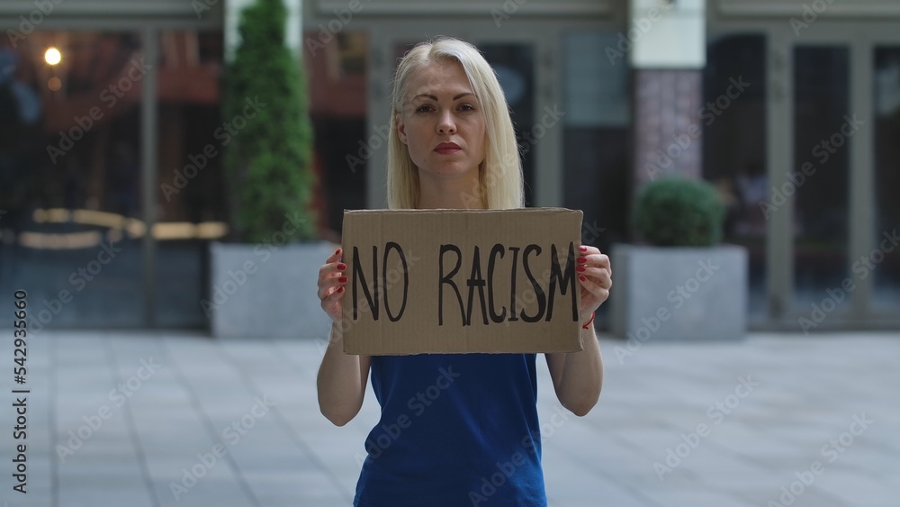 Young woman stands with a cardboard poster NO RACISM in a public place ...
