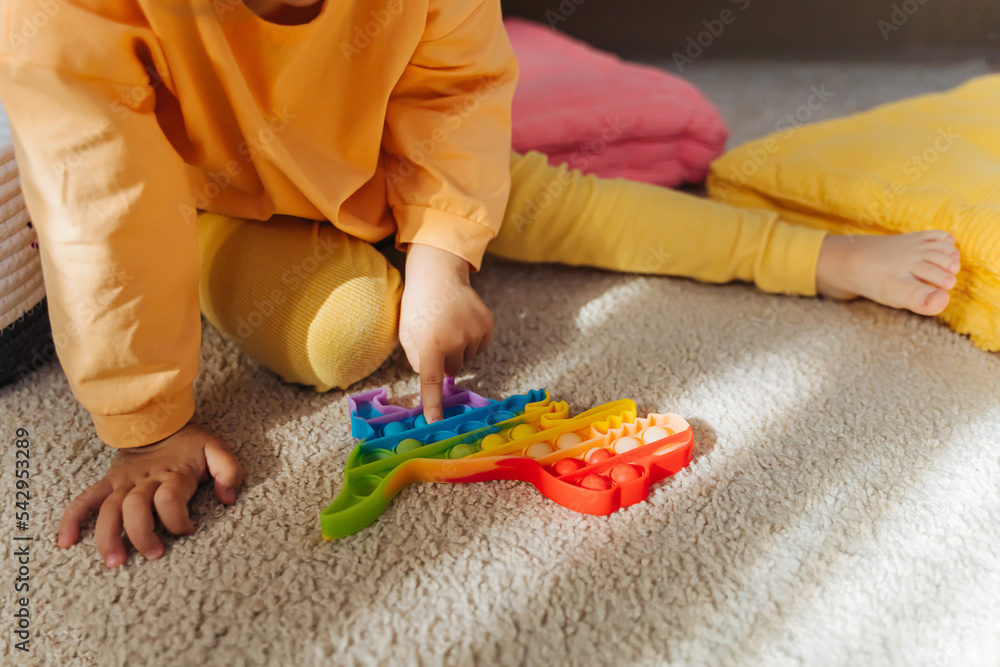 Child sitting on floor playing with the Pop It in childrens room. Push ...