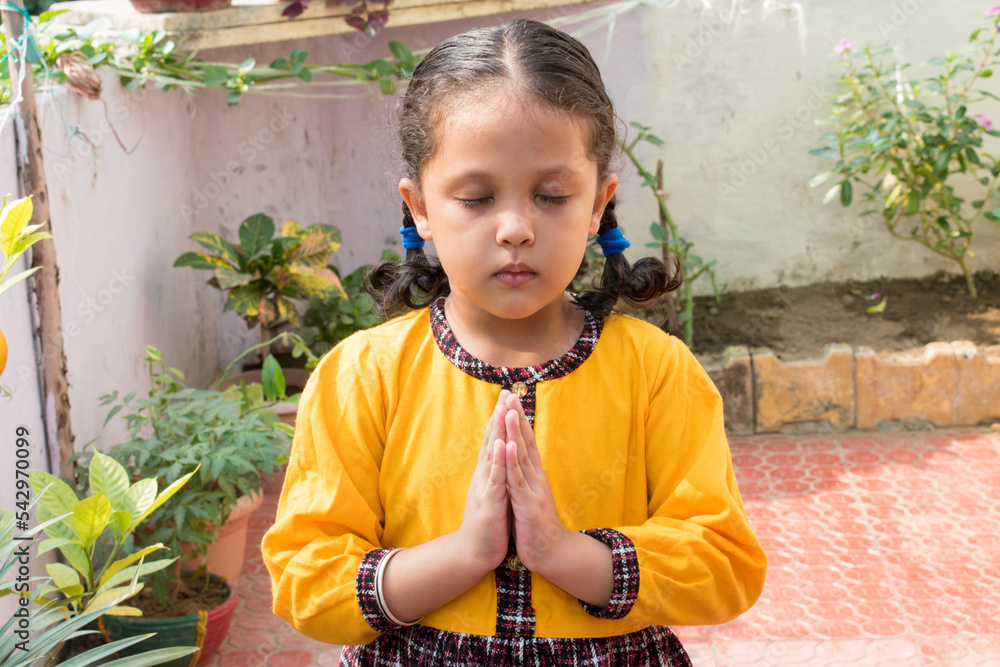 Indian girl in yellow and black frock holding palms together in Namaste ...