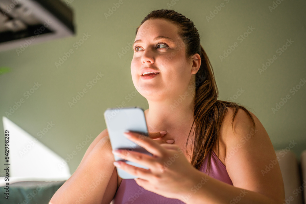 Positive girl with excess weight smiling with phone at her hands while ...