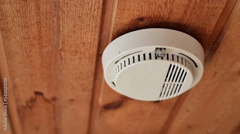 White fire alarm and smoke detector on ceiling in home brown wooden ...