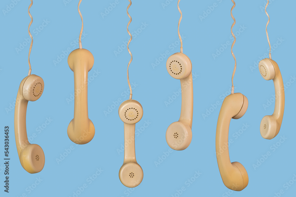 Many old telephone handsets from rotary landlines hanging from cords on ...