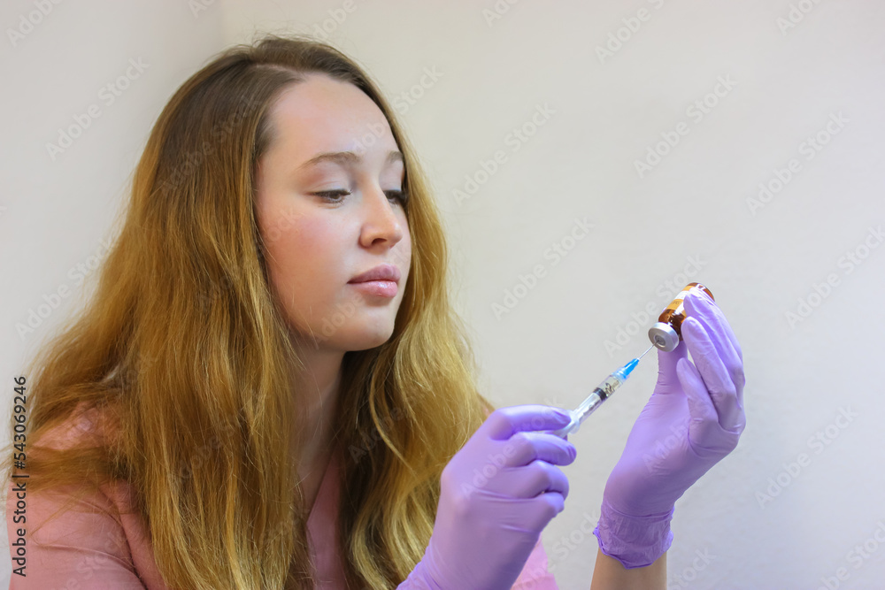 A young woman doctor wearing purple rubber gloves holds an injection ...