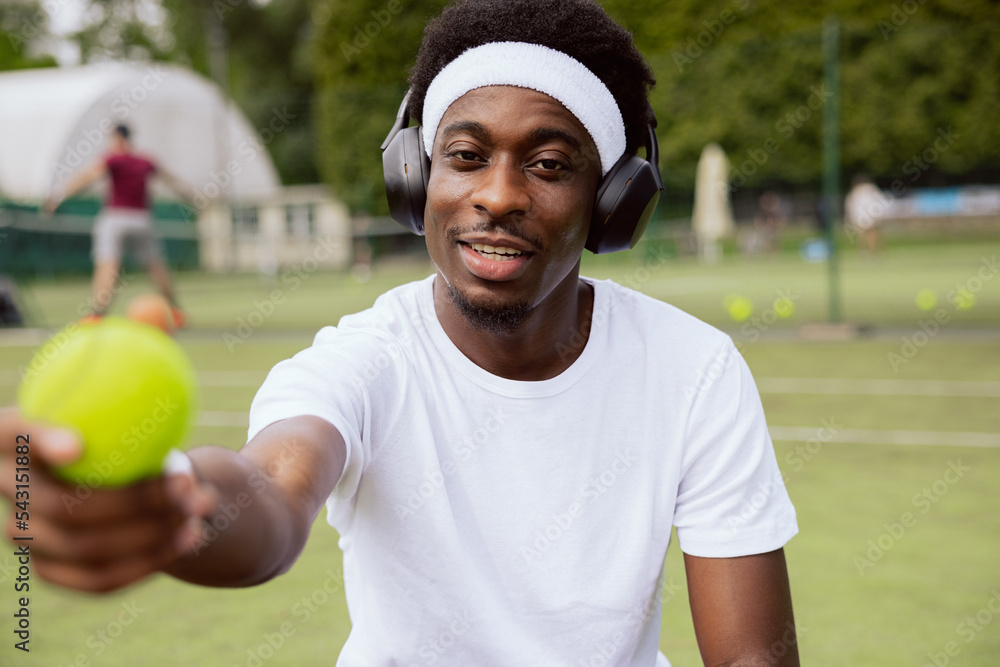 Attractive man of African appearance is sitting on grass of tennis ...