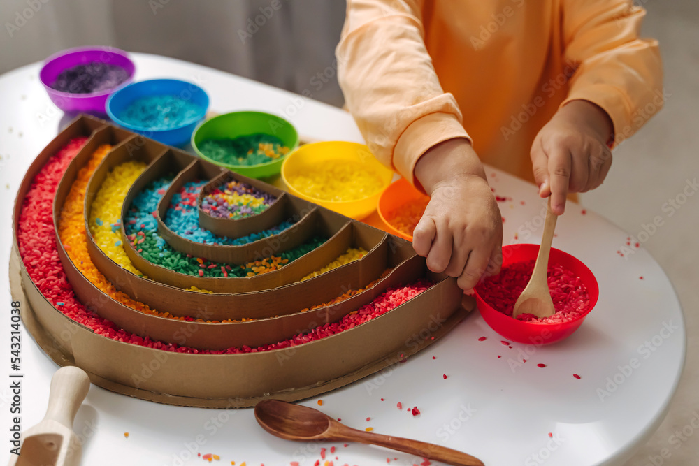Child hands playing colored rice and make rainbow. Child filled the ...
