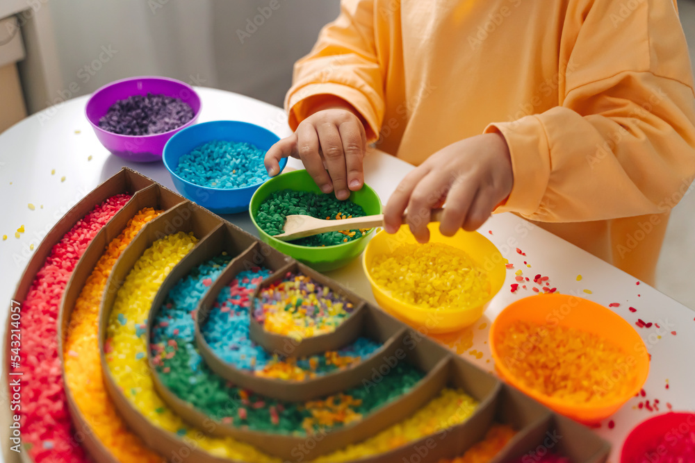Child hands playing colored rice and make rainbow. Child filled the ...