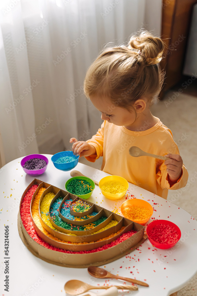 A little girl playing colored rice and make rainbow. Child filled the ...