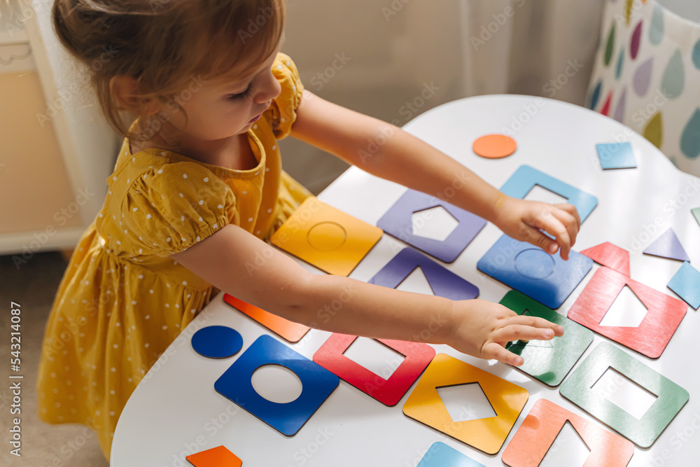 A little girl playing with wooden shape sorter toy on the table in ...