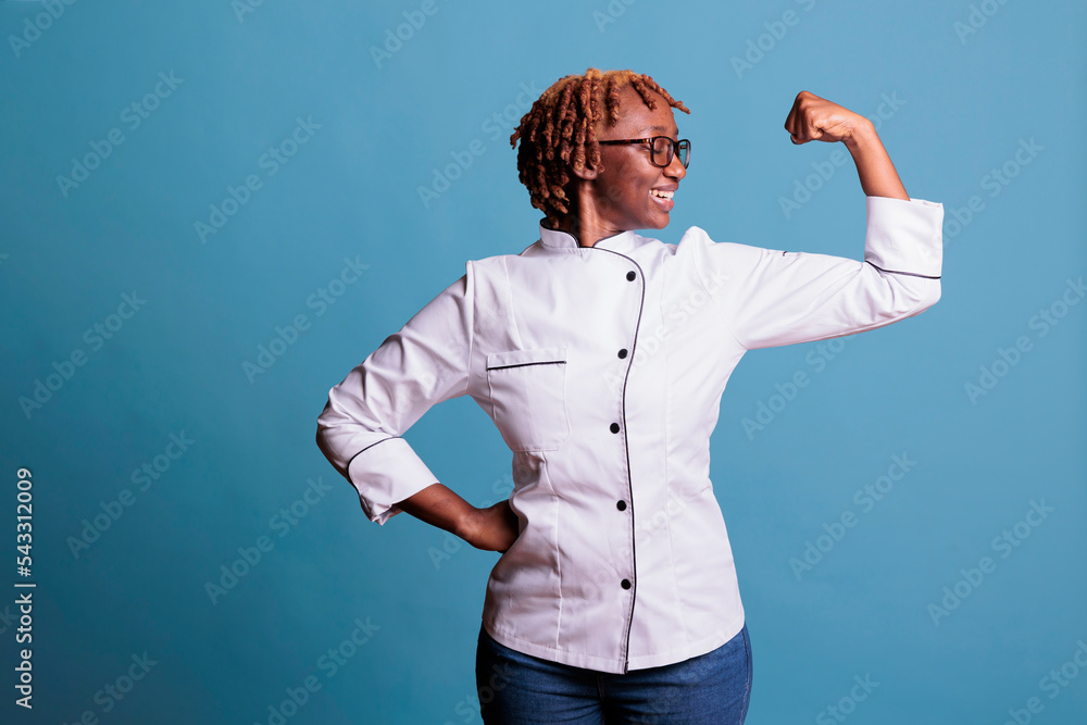 Female kitchen staff member wearing chef jacket smiling as looks at arm ...