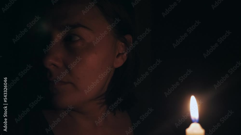 A Caucasian woman in a dark room with a candle in her hands looks ...