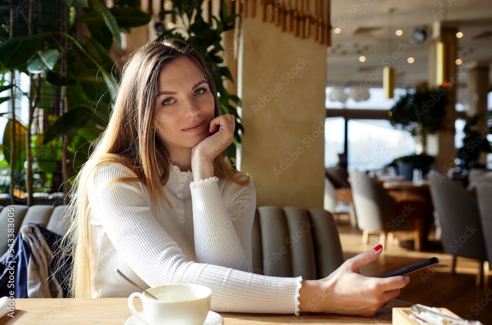 Beautiful woman sitting in cafe. Coffee break. Morning light falls from ...