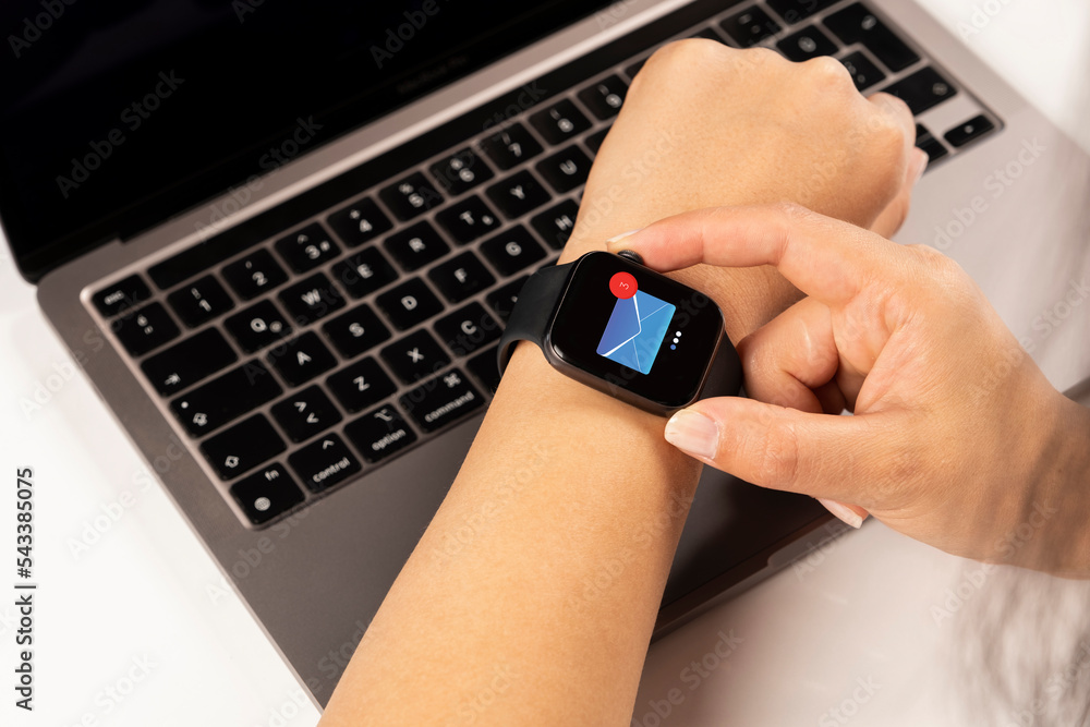 Email icon on smartwatch screen, woman hand over laptop touching email ...