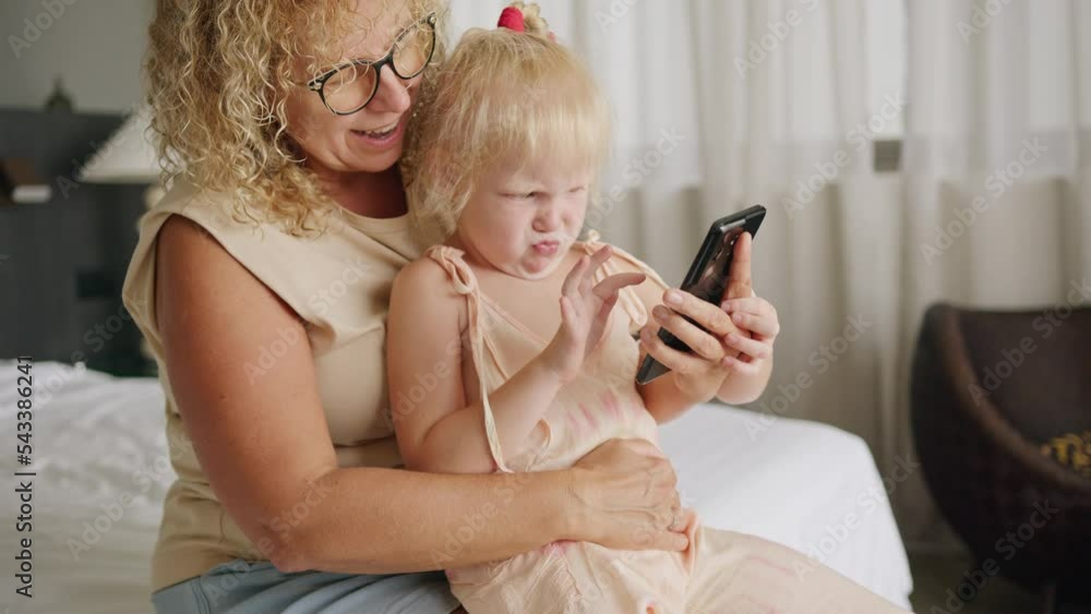Curly blonde grandma teaches a small preschool cute child girl to use a ...