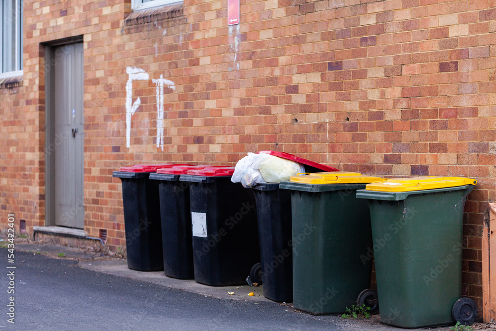 Overflowing trash in rubbish bin lined up on wall Stock Photo | Adobe Stock