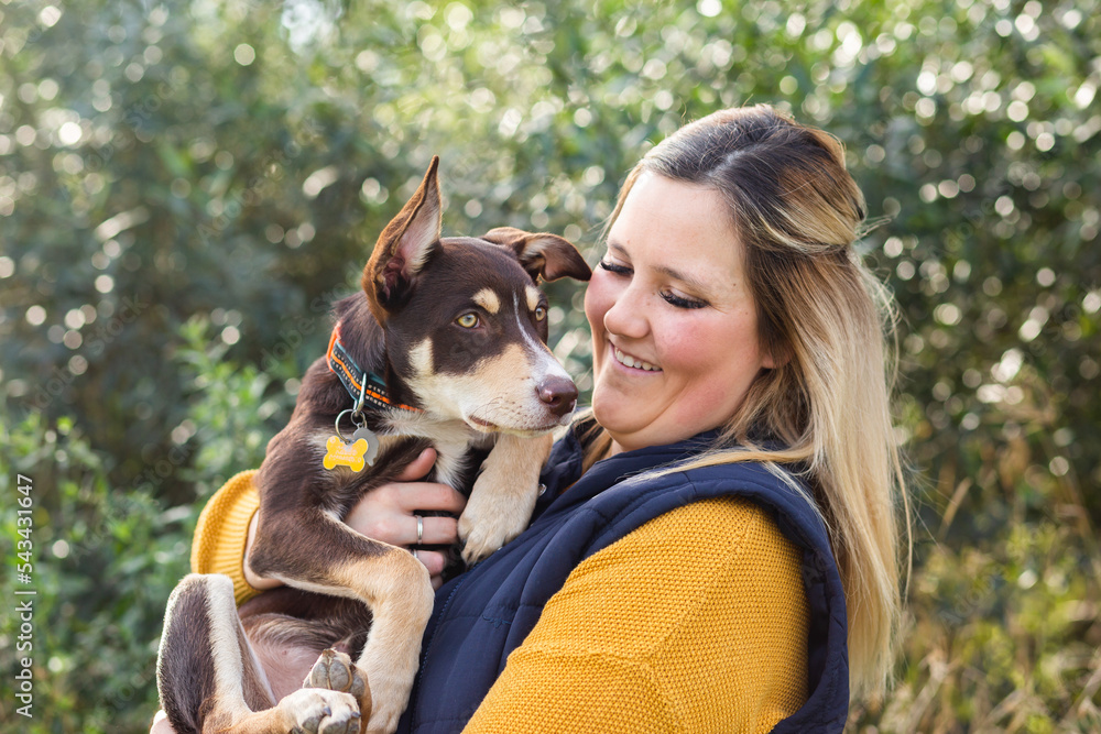 Smiling young woman holding her pet Australian Kelpie puppy dog with ...