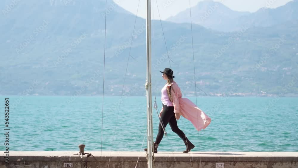 Vidéo Stock Woman walks on pier at lake Garda against giant forestry ...
