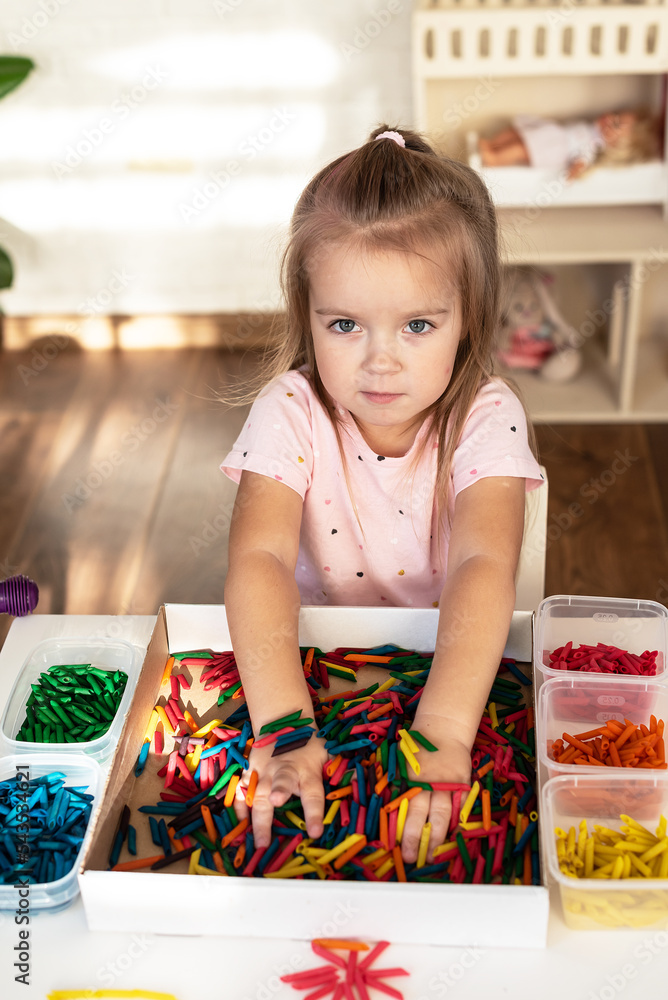 Little girl toddler playing with sensory bin with colored dyed pasta ...