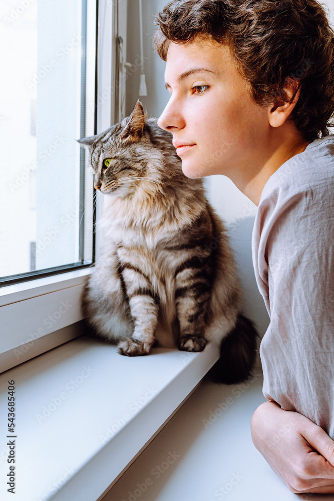 Attractive teenage girl next to beloved cat hugging while looking out ...