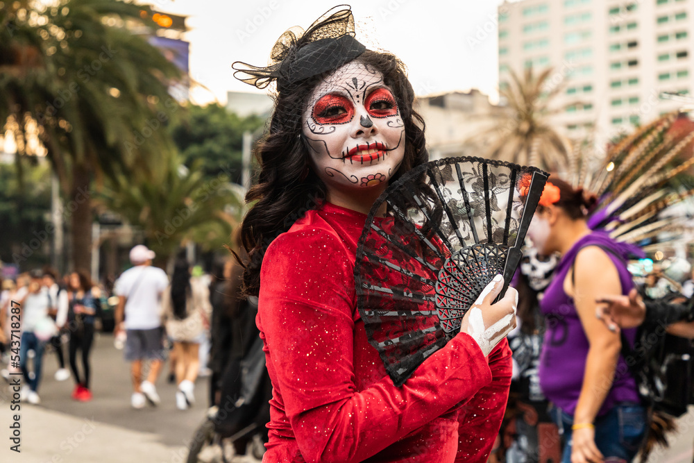 Mujer joven caracterizada como catrina con abanico negro y vestido rojo ...