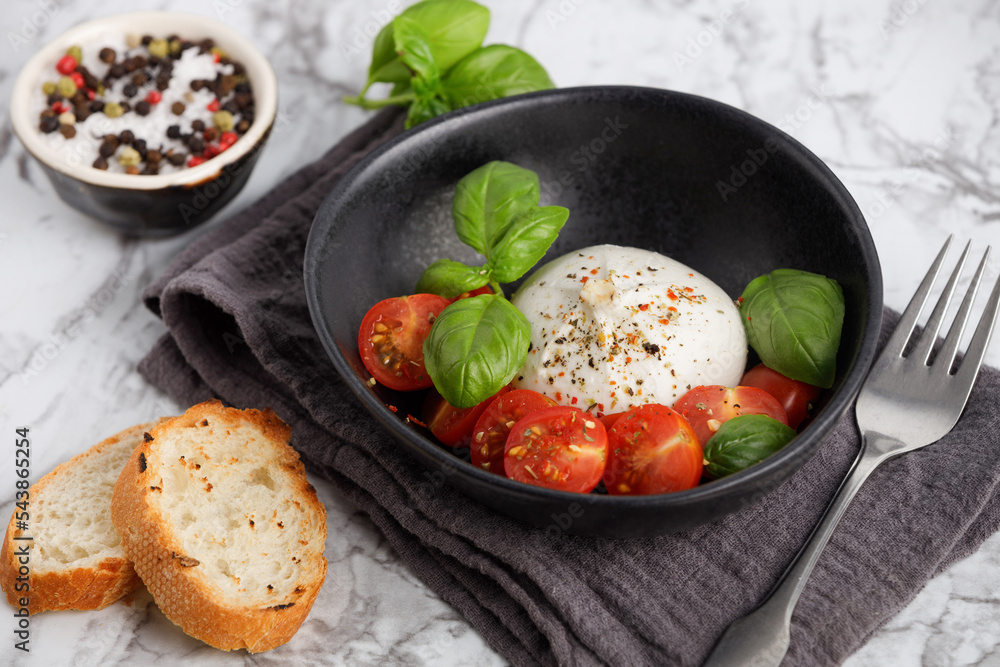 Fresh Italian burrata with tomatoes and basil on plate on marble table ...
