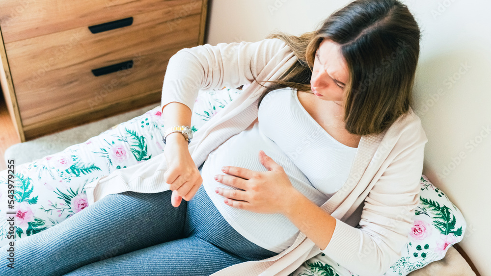 Pregnant pain contractions. Pregnant woman watching clock, holding baby ...
