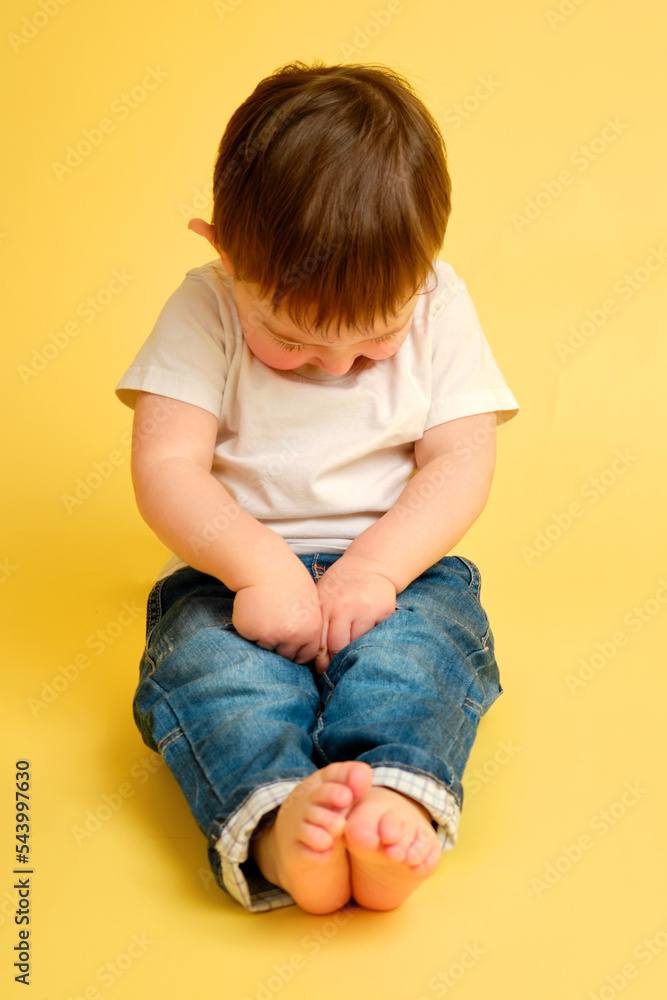 Full length portrait of an embarrassed toddler baby on a studio yellow ...