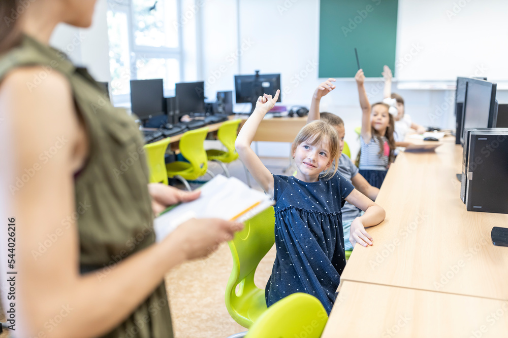 Students with hand raised looking at teacher standing in class at ...