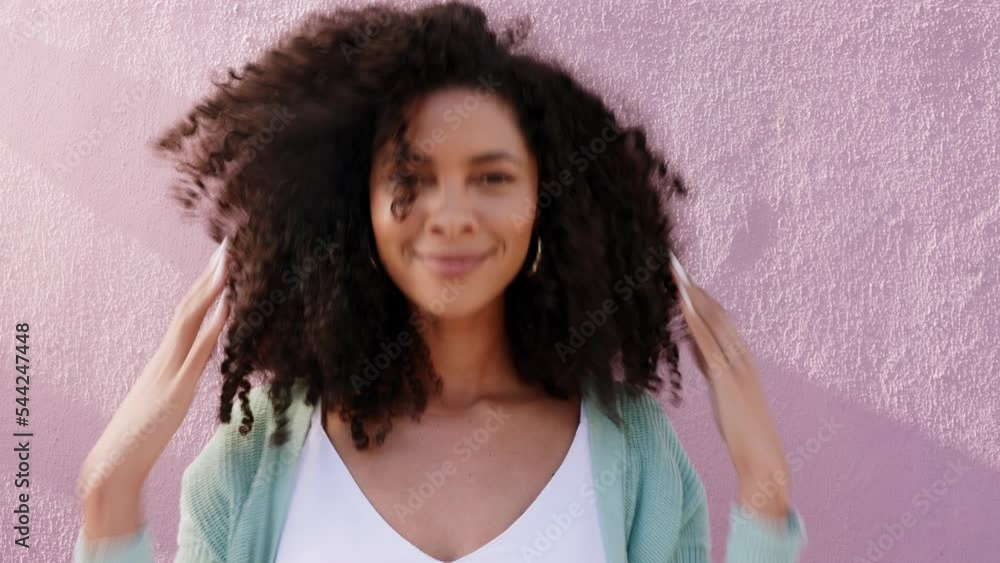 Portrait of black woman touching her afro outdoor by a pink wall while ...