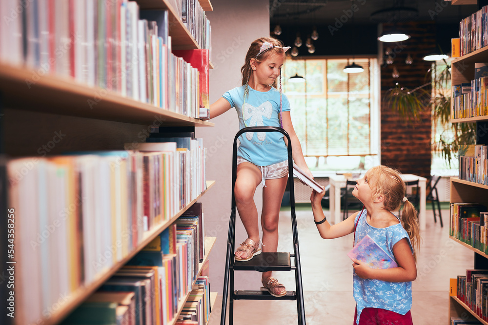 Two schoolgirls choosing books in school library. Primary school ...