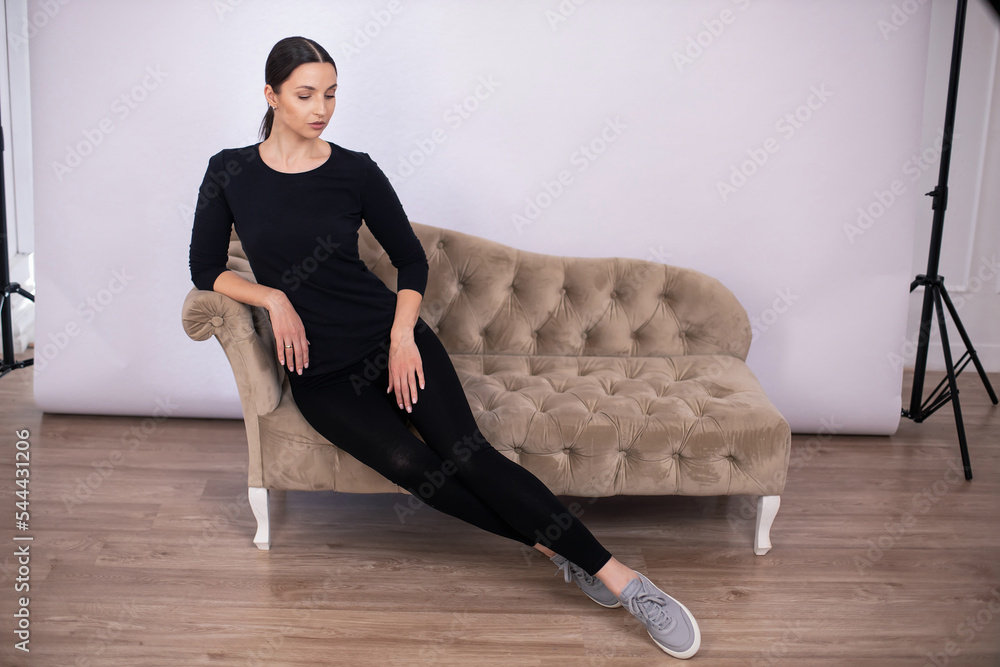 full length woman poses on a sofa in black tight fitting clothes and ...