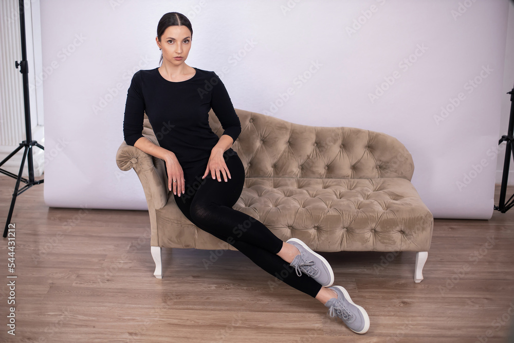 full length woman poses on a sofa in black tight fitting clothes and ...