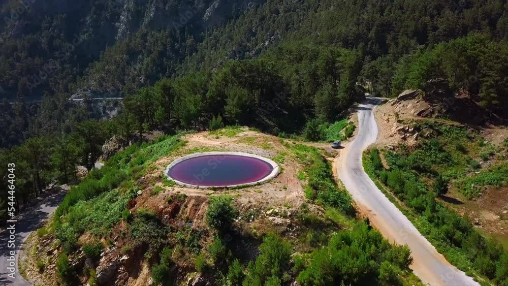 Aerial view of a round shaped red lake located at the edge of a green ...