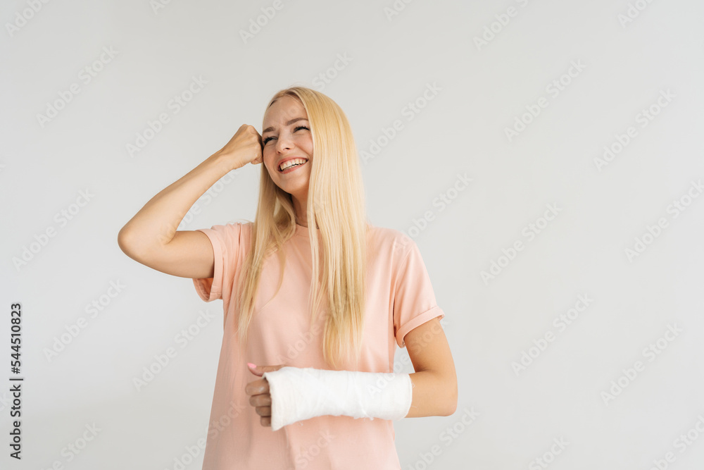 Studio portrait of cheerful young woman with broken arm wrapped in ...