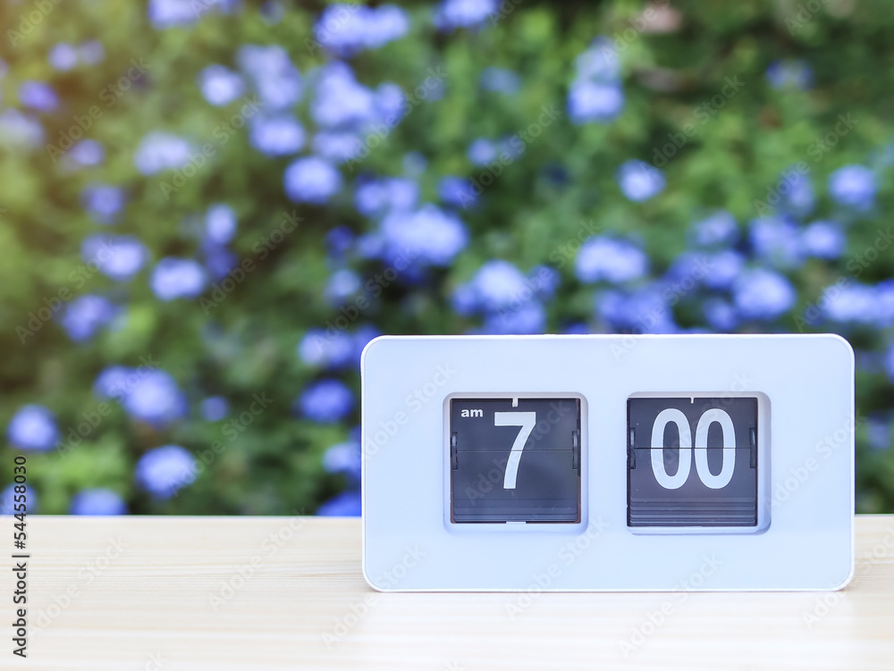 white flip clock showing 7.00 o clock on the table in the garden with ...