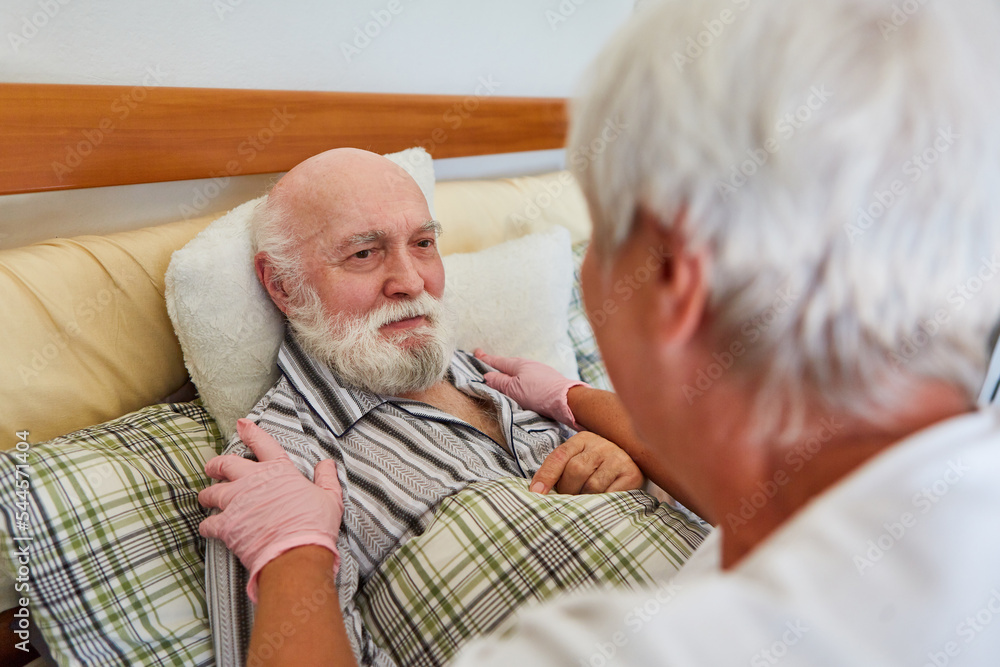 Geriatric nurse comforts old man in bed in nursing home Stock Photo ...