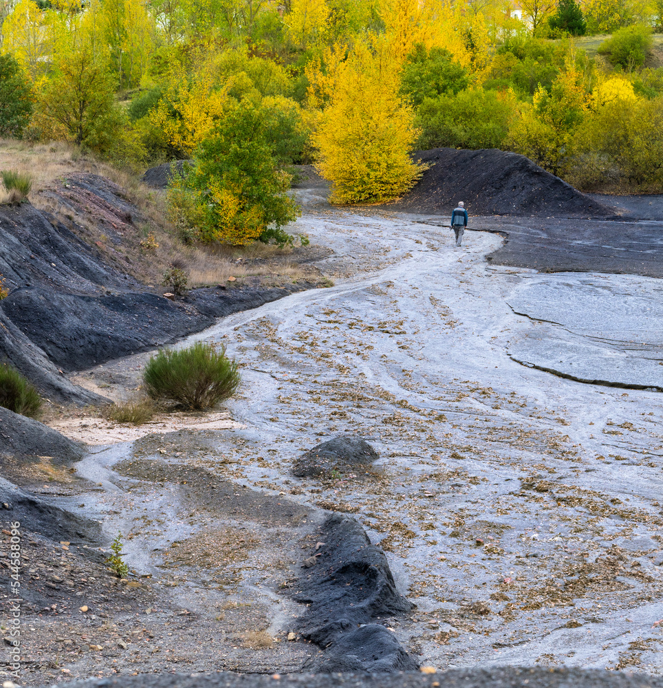 Man walking throught a path made by coal waste nea a village surrounded ...
