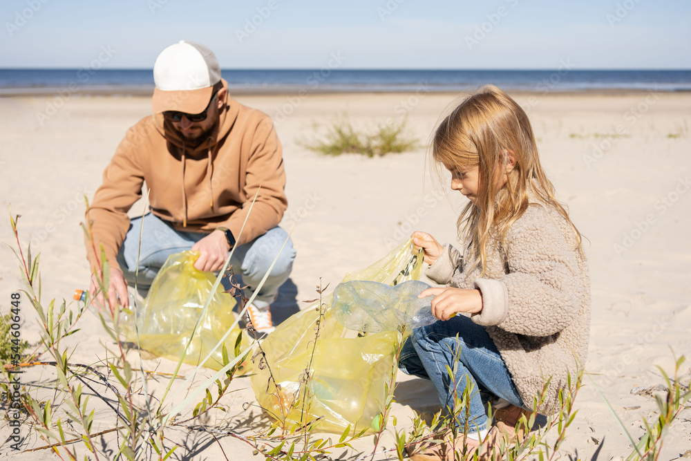 Dad and daughter cleaning up the beach pick up plastic bags that ...