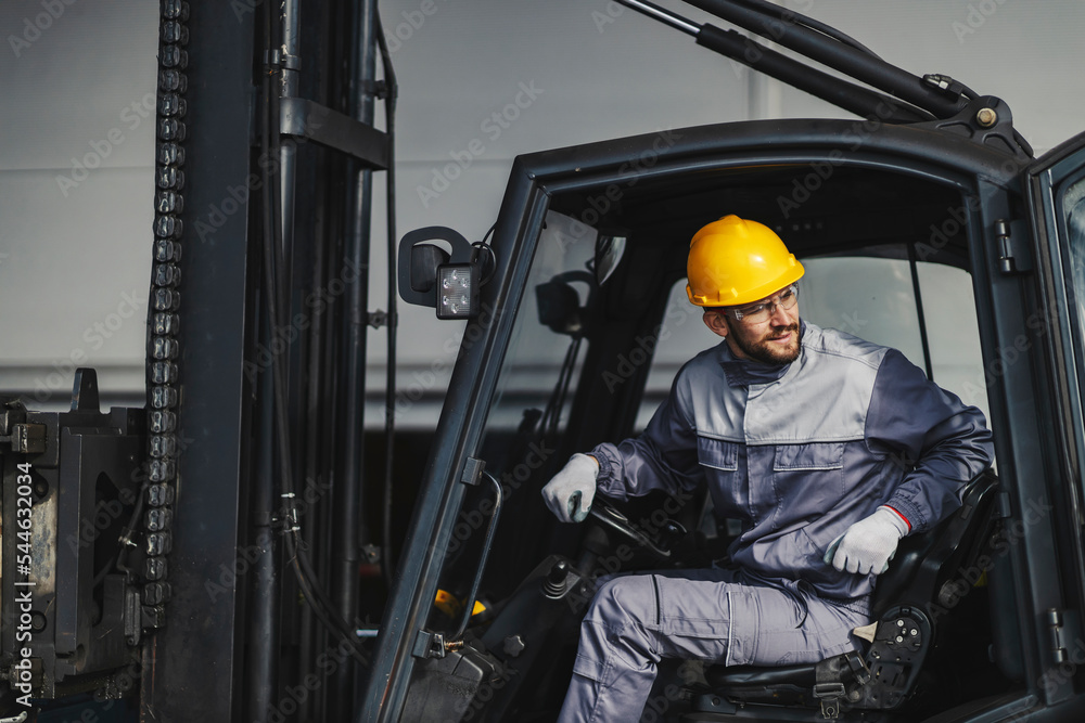 A forklift driver looks over the shoulder while driving a forklift in a ...