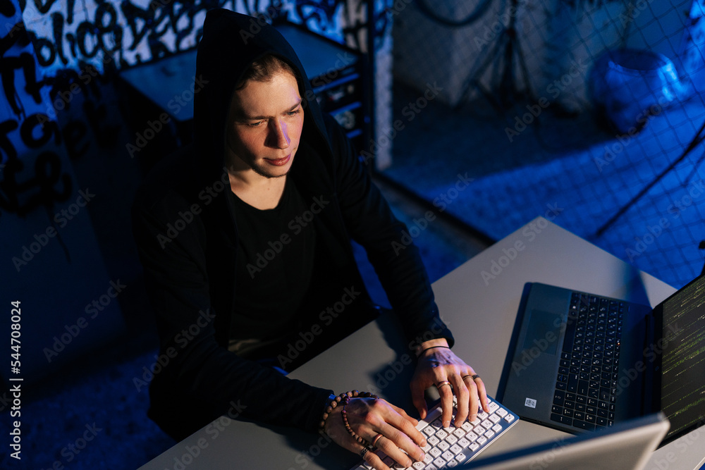 High-angle side view of dangerous hacker man wearing hooded typing code ...