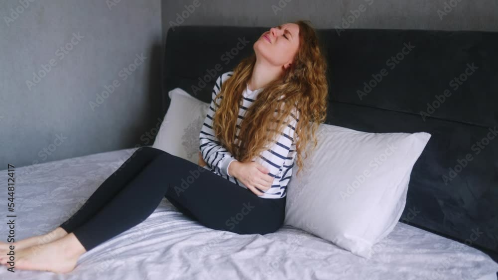 Caucasian woman suffering from severe stomach ache sitting on bed in ...