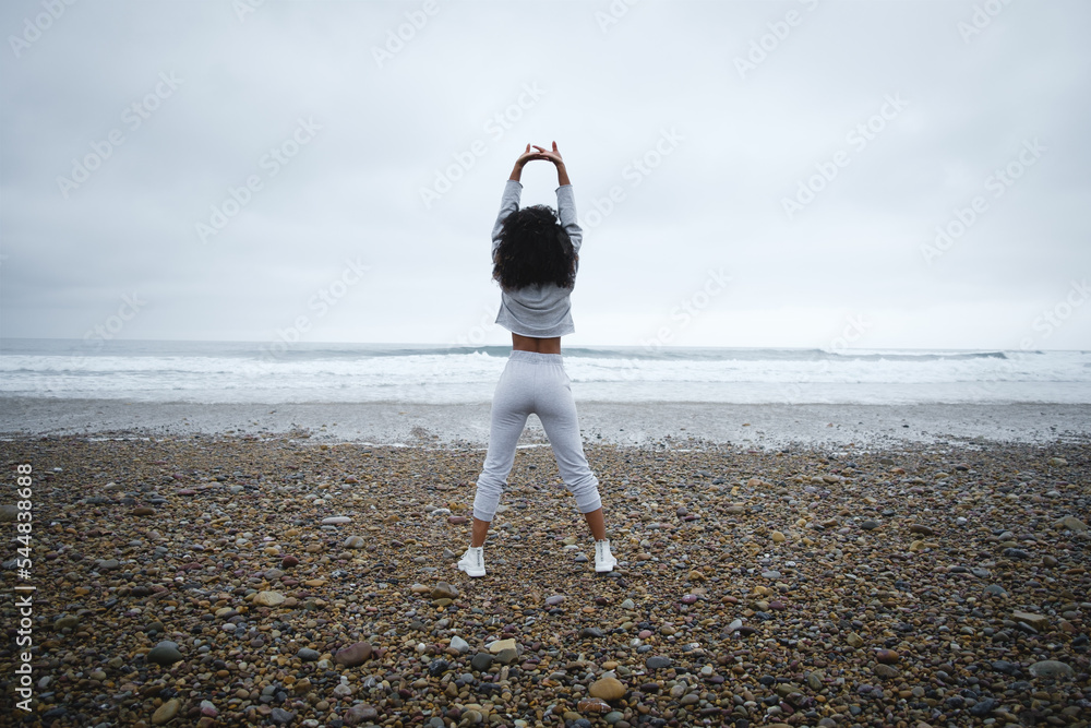 Fitness woman working out and stretching at the beach towards the sea ...