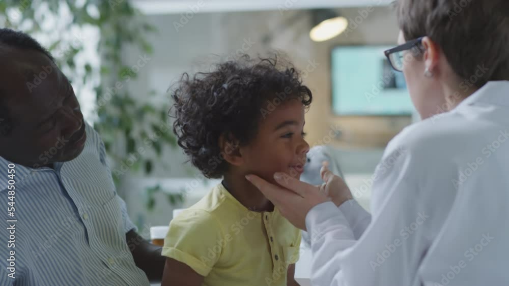 Little African American kid sitting with father while female doctor ...