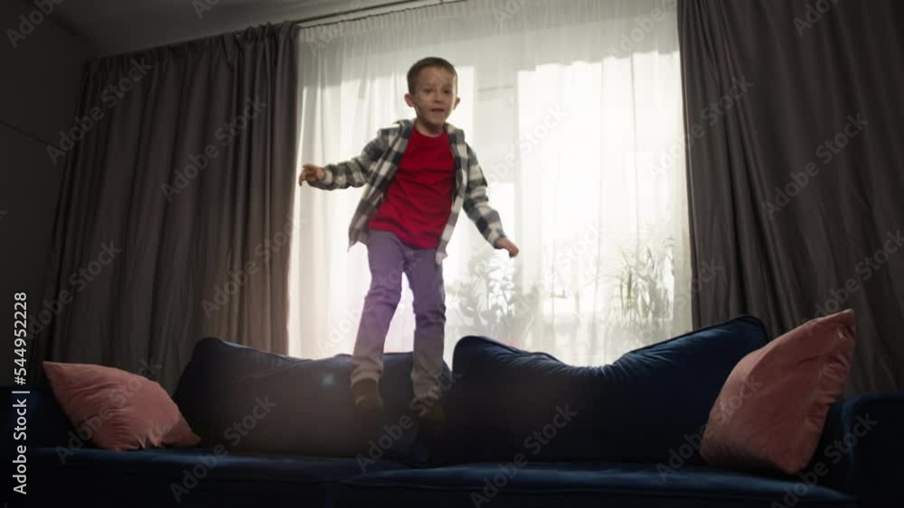 Slow motion video of Caucasian boy jumping on couch in living room. The ...