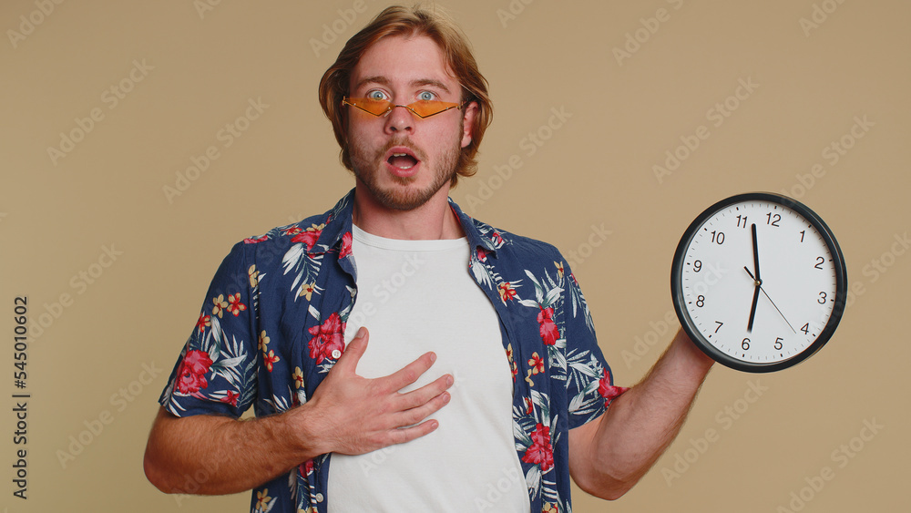 Confused young man with anxiety checking time on clock, running late to ...