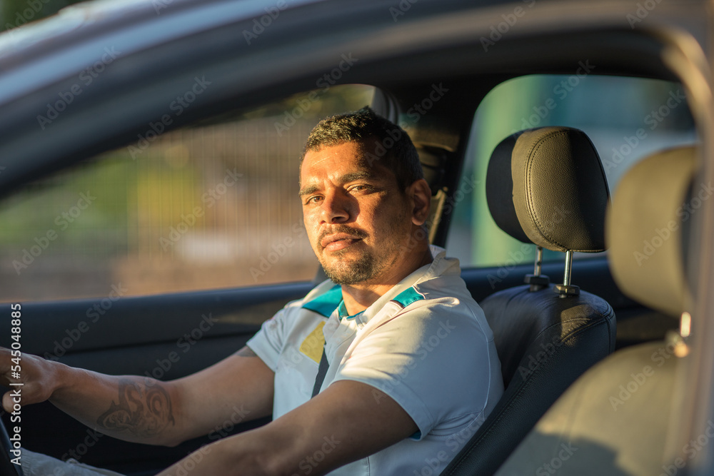 Aboriginal man seen through passenger window driving a car with dark ...
