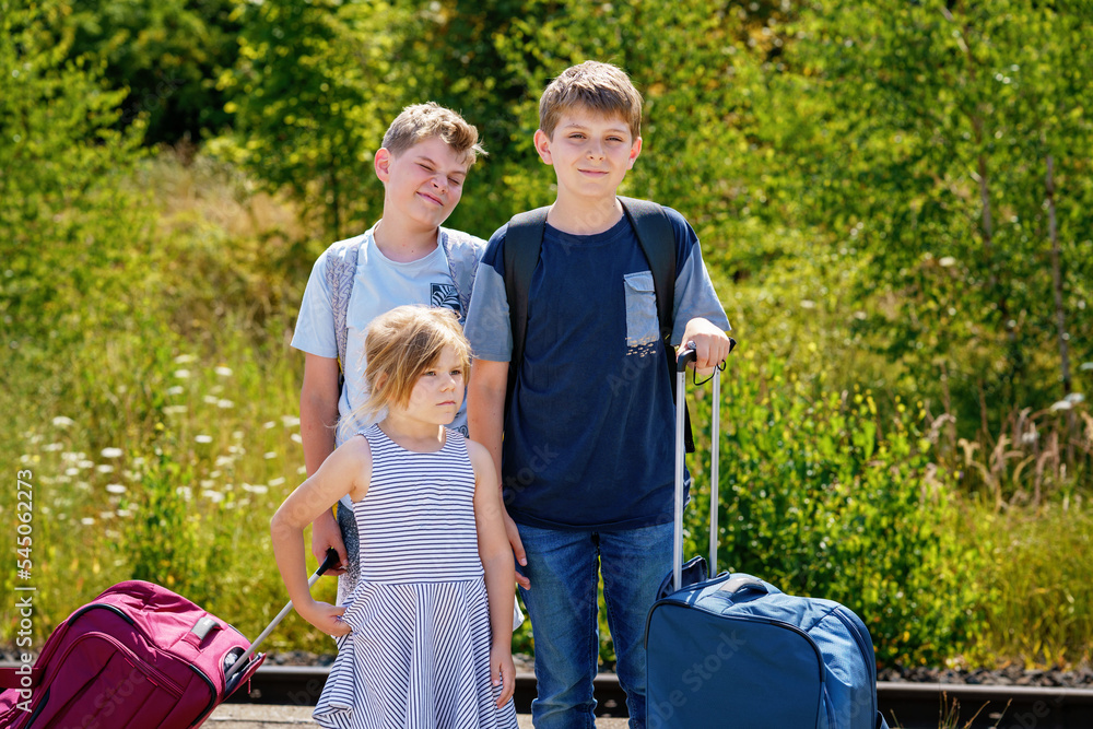 Three children, school boys and preschool girl with suitcases before ...