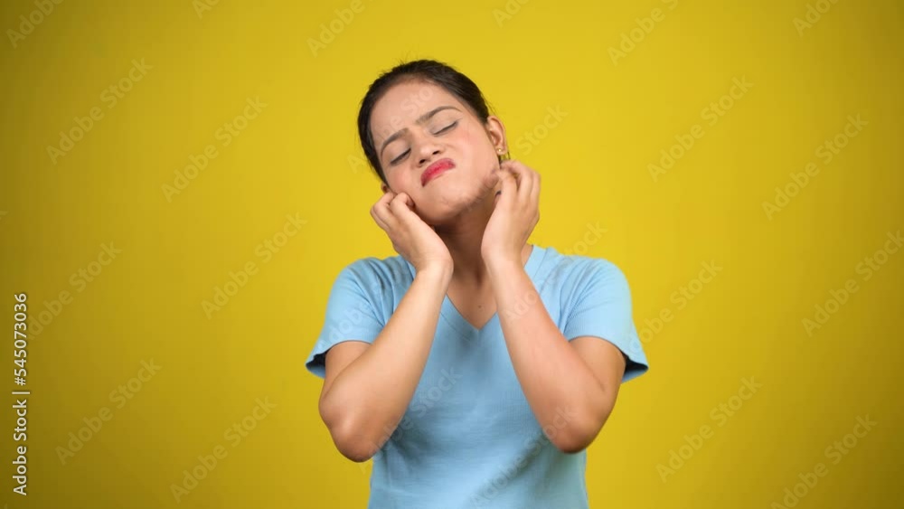 Young woman scratching face or cheek, isolated over yellow background ...