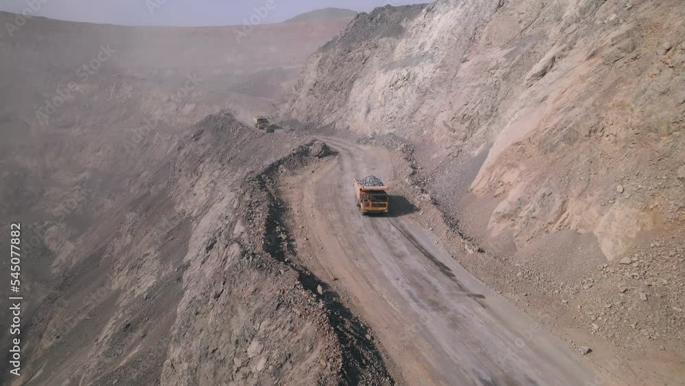 Two yellow quarry trucks one behind another one loaded with stones are ...