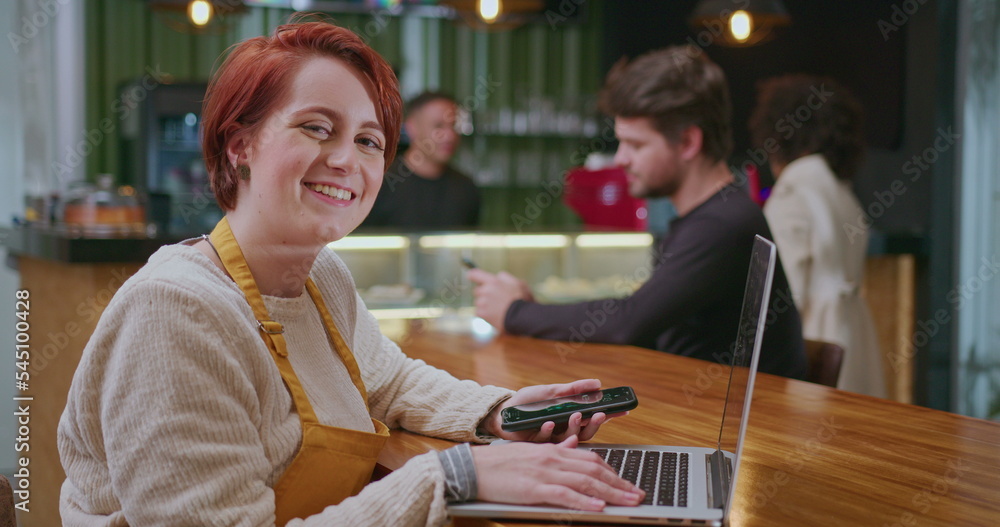 One happy female barista seated at coffee shop table holding phone in ...