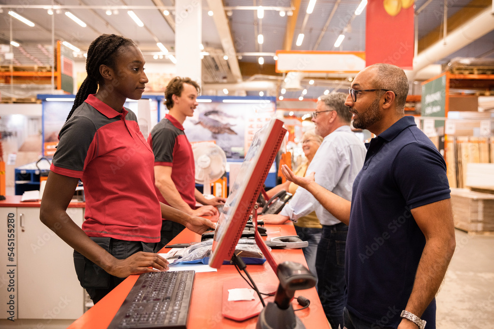 Male customer gesturing and talking with female cashier while standing ...